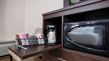 Um micro-ondas e máquina de café sobre um balcão de madeira, com uma cesta contendo saquinhos de chá e outros objetos.