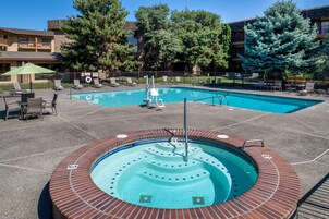 Uma piscina com hidromassagem, espreguiçadeiras e uma área cercada por árvores.