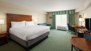 Quarto de hotel com uma cama grande, uma escrivaninha, uma cadeira, uma televisão e uma janela com cortinas.