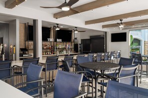 Uma área de bar com diversos tipos de assentos, balcão com vários frascos e ventiladores de teto.