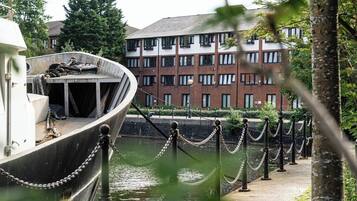 Um canal com um barco atracado à esquerda, uma passarela para pedestres e um edifício ao fundo.
