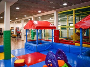 Espa ço de recreação infantil com estruturas acolchoadas, piscina de bolinhas e jogos de fliperama.