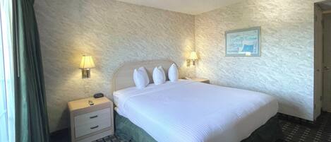 Quarto de hotel com uma cama, duas mesas de cabeceira com luminárias, um quadro na parede e um tapete estampado.