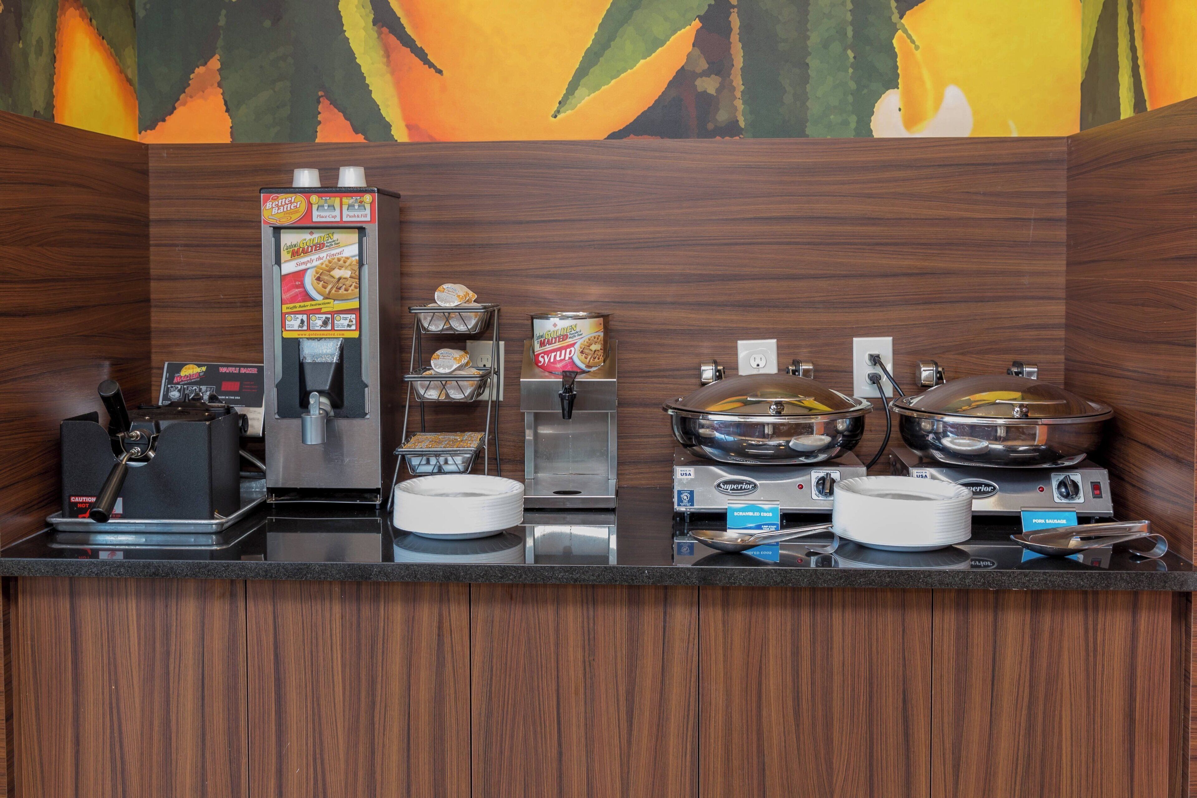 Disposição de buffet com máquina de café, dispensador de xarope e estações de comida quente.