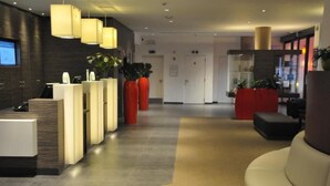 Um hall de hotel moderno com balcão de recepção, área de estar e uma grande planta.