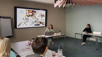 Uma sala de conferências com um ecrã grande exibindo um plano, uma lousa e um projetor.