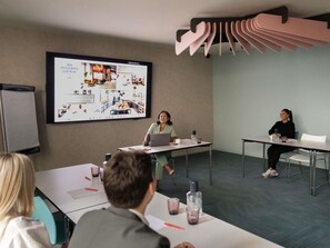 Uma sala de conferências com um ecrã grande exibindo um plano, uma lousa e um projetor.
