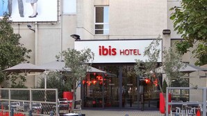 Exterior do hotel ibis com fachada de vidro, área de estar externa e esquema de cores vermelho e branco.