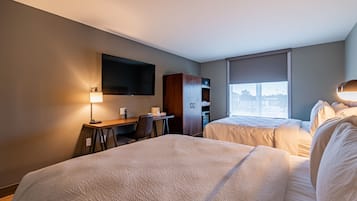 Quarto de hotel com duas camas, uma escrivaninha, uma cadeira, televisão na parede e janela com vista.