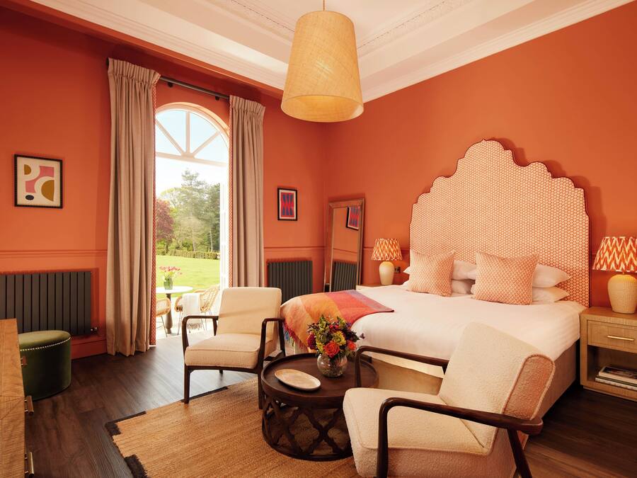 Quarto com cama grande, duas cadeiras, uma mesinha e vista para o exterior.