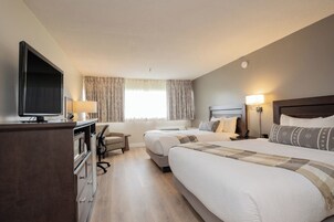 Quarto de hotel com duas camas, televisão, escrivaninha e uma cadeira.