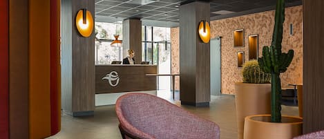 Uma área de recepção moderna com balcão, espaço para acomodar visitantes e plantas decorativas.