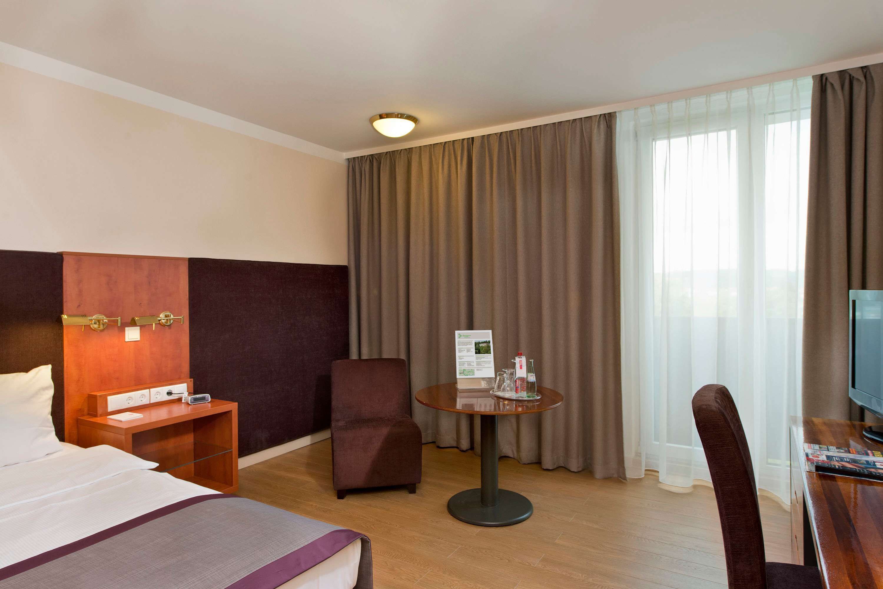 Quarto de hotel com uma cama, uma mesa de escritório, uma cadeira, uma pequena mesa com um aviso e uma televisão.