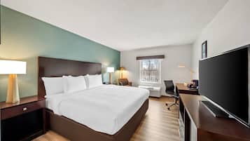 Quarto de hotel com cama, mesas de cabeceira, escrivaninha com televisão, cadeira e janela.