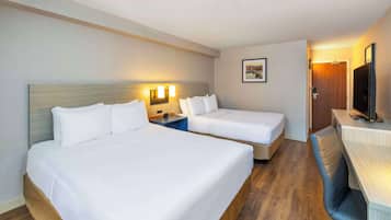 Quarto de hotel com duas camas, uma escrivaninha, uma cadeira, televisão e um quadro na parede.