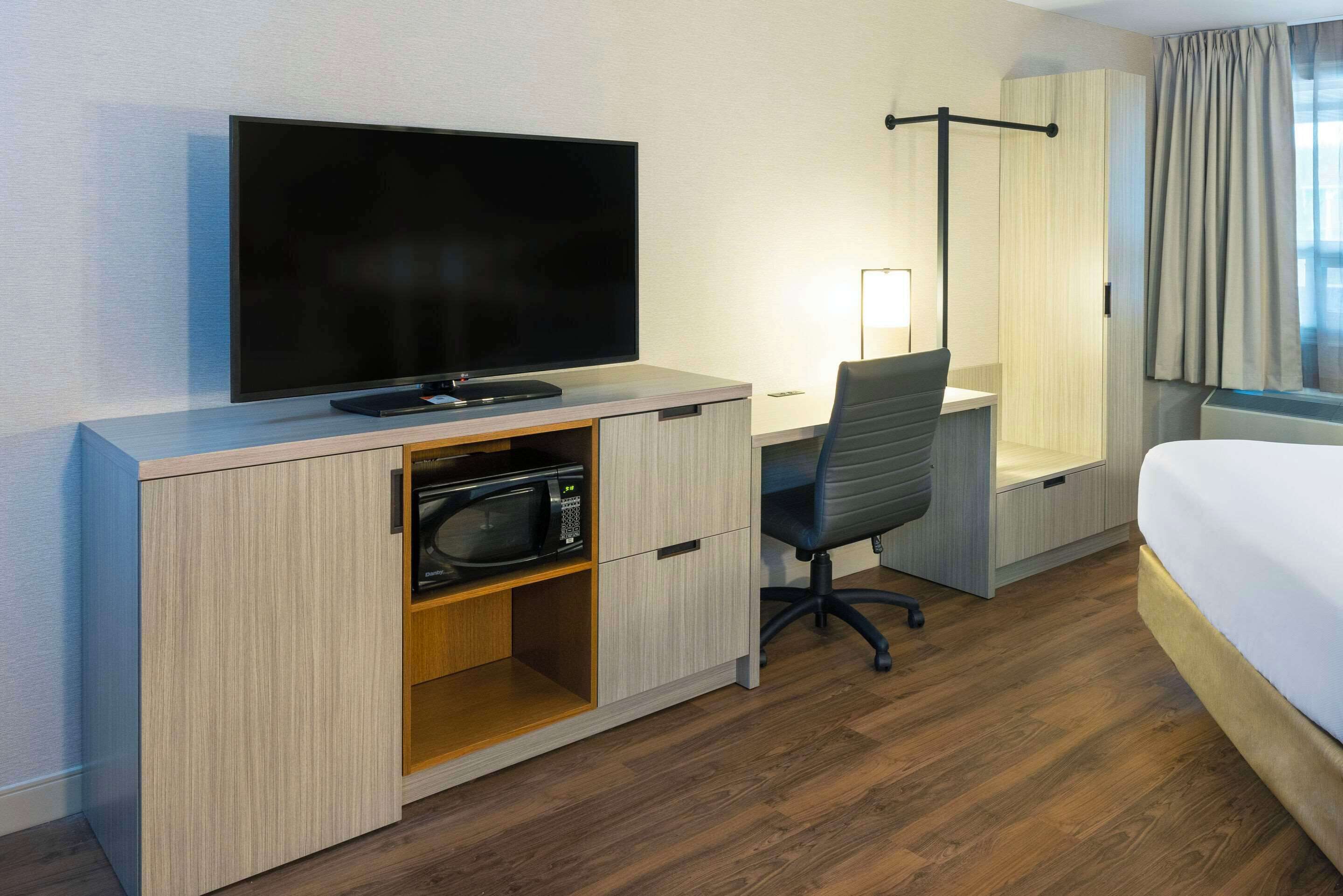 Quarto de hotel com televisão de tela plana, uma escrivaninha com cadeira, micro-ondas e uma cama.