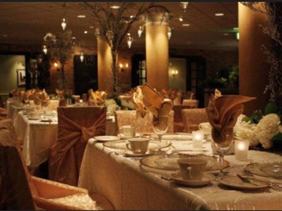 Uma sala de banquetes com mesas redondas preparadas para refeições, com toalhas brancas e centros de mesa com velas.
