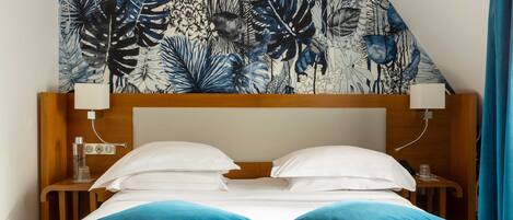 Quarto de hotel com cama, duas almofadas, cabeceira, mesas de cabeceira e tapeçaria na parede.