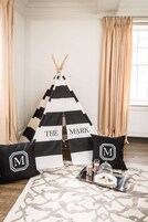 Quarto aconchegante com um tipi listrado em preto e branco, um tabuleiro com lanches e bebidas, e almofadas combinando com um monograma.
