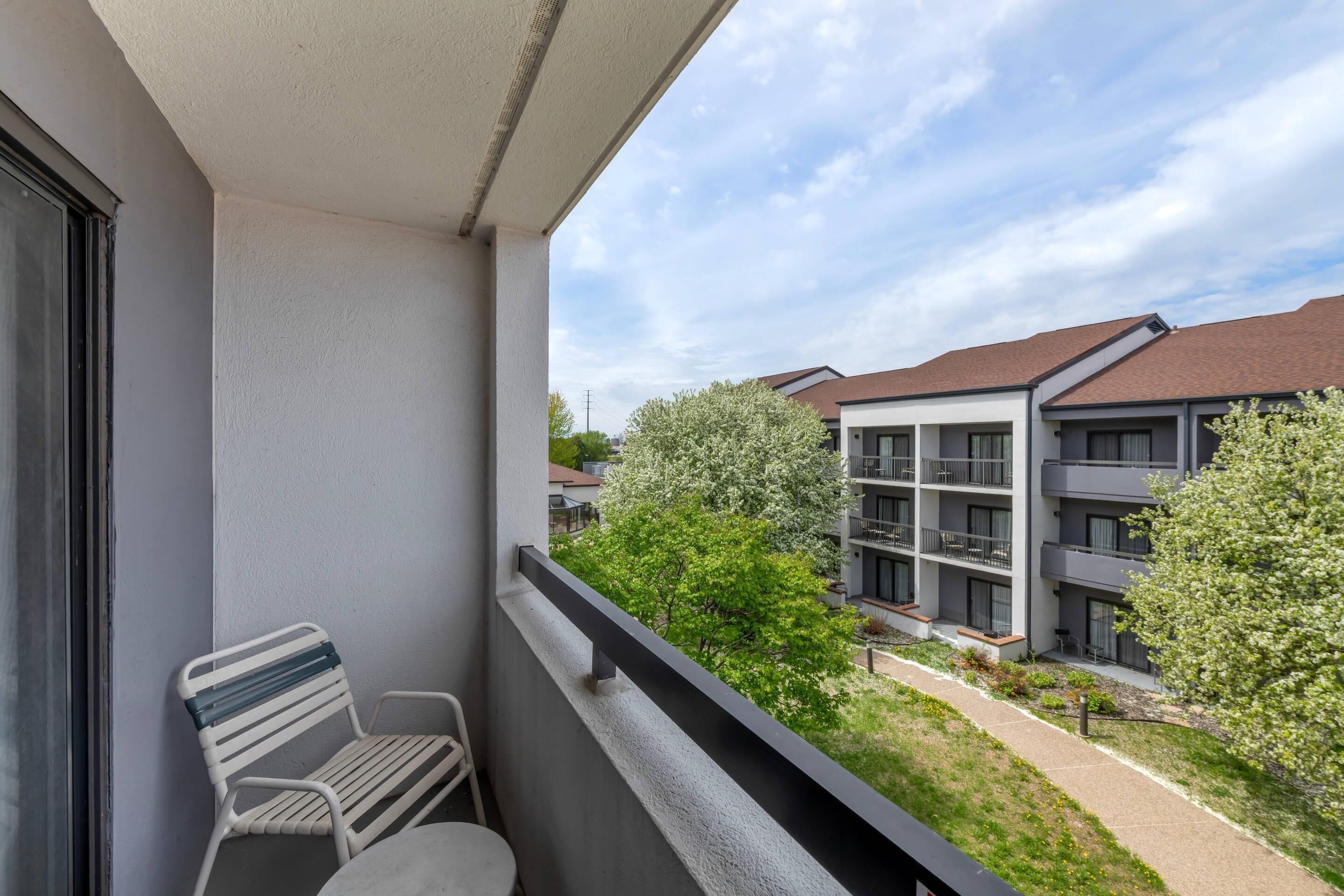 Varanda com cadeira e mesa, com vista para uma área residencial com edifícios modernos e áreas verdes.