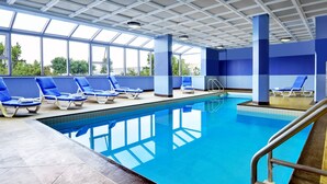 Uma piscina interior com água azul cristalina, rodeada por espreguiçadeiras azuis e um chão em mosaico.
