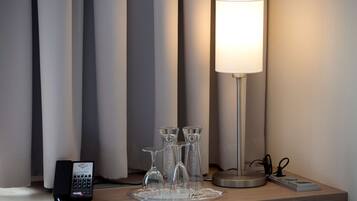 Quarto de hotel com mesa de cabeceira que inclui telefone, abajur e bandeja com três vasos de vidro transparente.