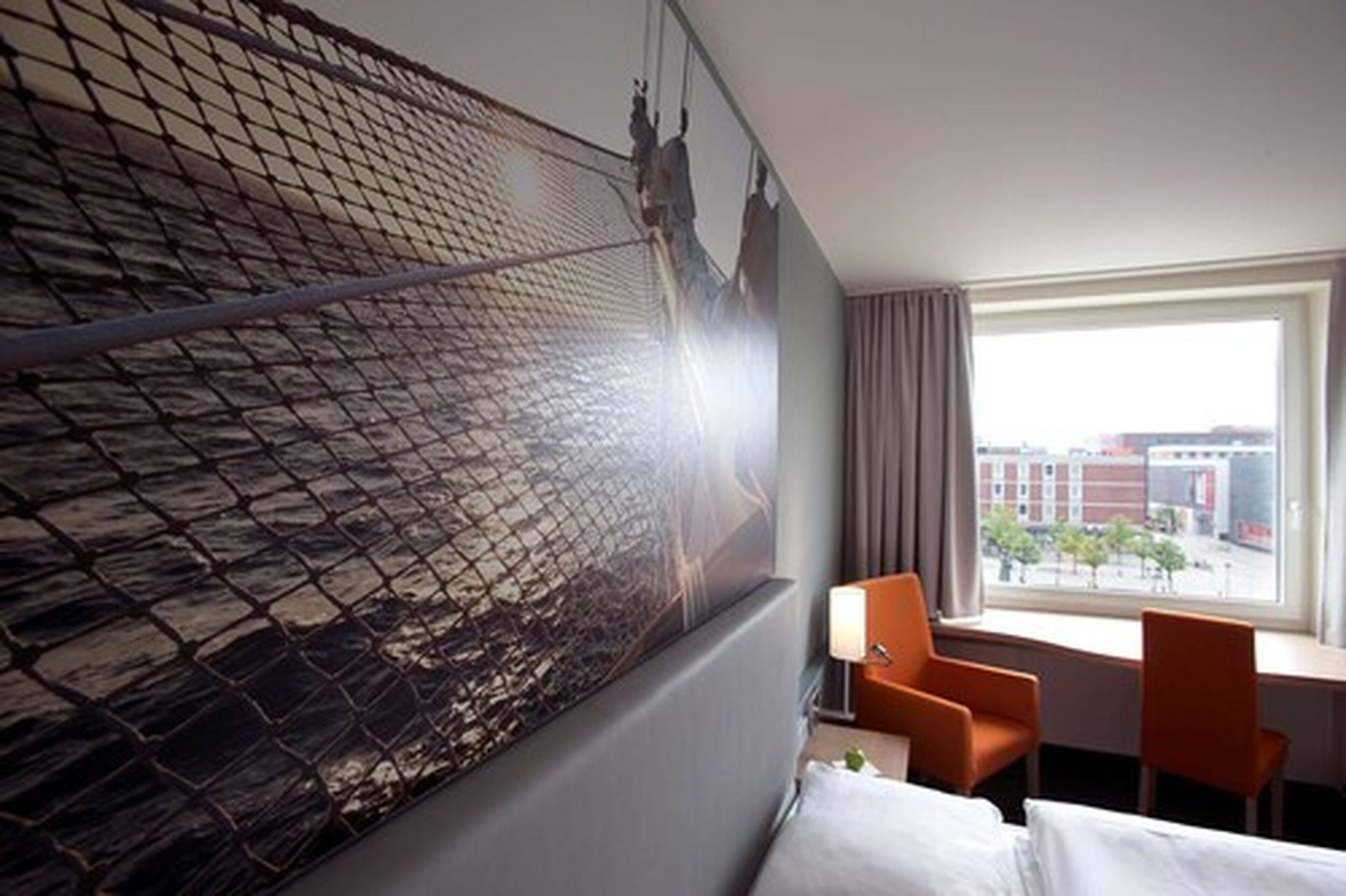 Quarto de hotel com uma cama, uma escrivaninha e uma cadeira. Há uma janela com vista para edifícios.