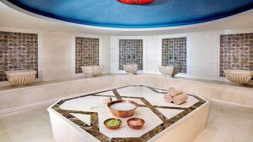 Um quarto de spa com uma banheira de mármore central, taças decorativas e paredes com azulejos estampados.