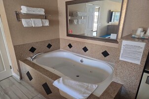 Casa de banho com banheira, um porta-toalhas com toalhas dobradas, espelho e sinal com instruções de segurança.