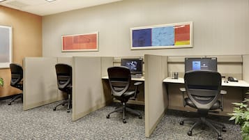 Espaço de cubículos de escritório com estações de trabalho individuais, cada uma com computador, cadeira e divisória.