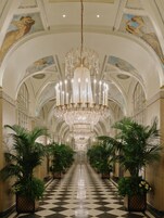 Um amplo salão com um grande lustre, tetos em arco e plantas em vasos.