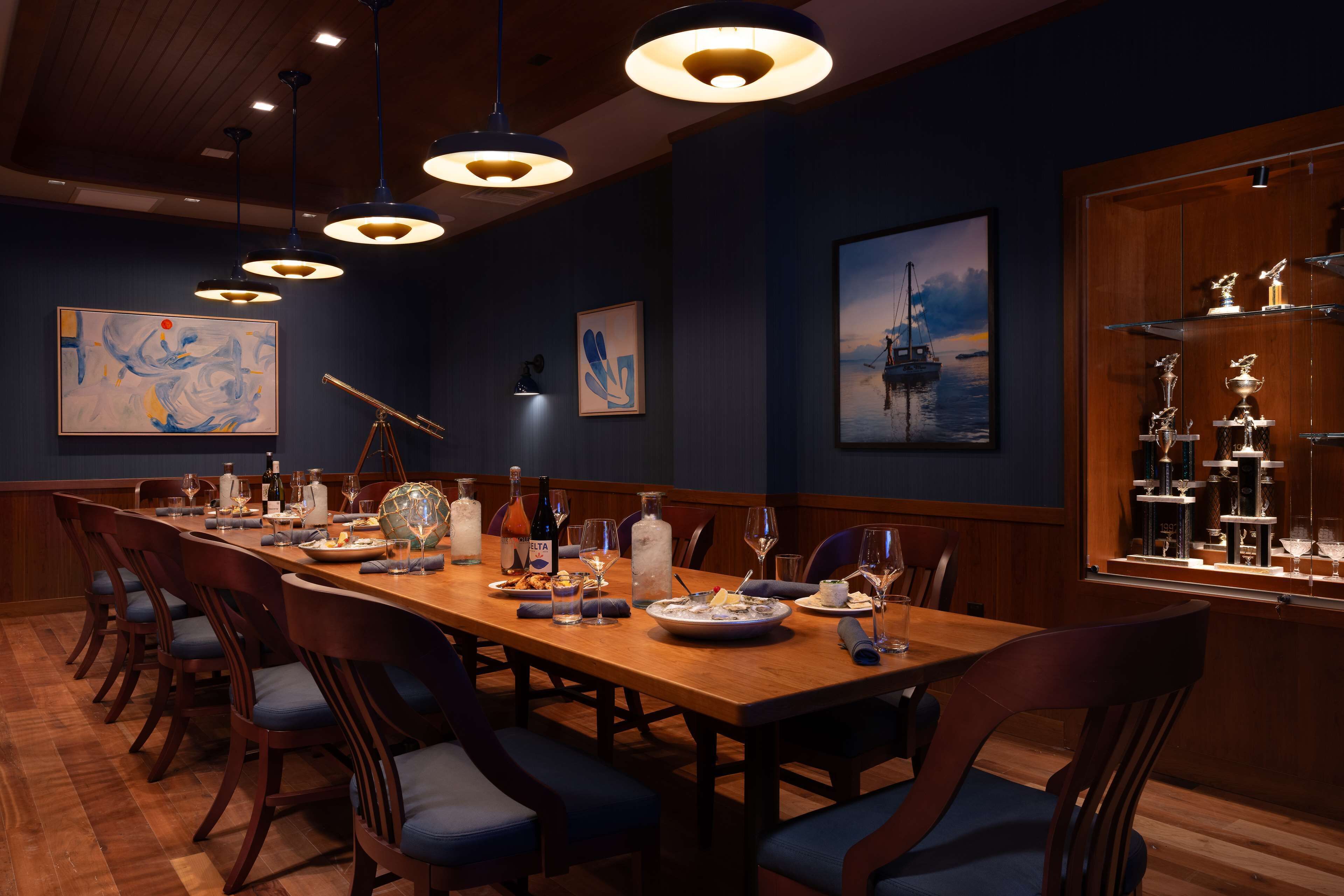 Uma sala de jantar com uma mesa de madeira comprida, várias cadeiras e luminárias pendentes.