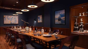 Uma sala de jantar com uma mesa de madeira comprida, várias cadeiras e luminárias pendentes.