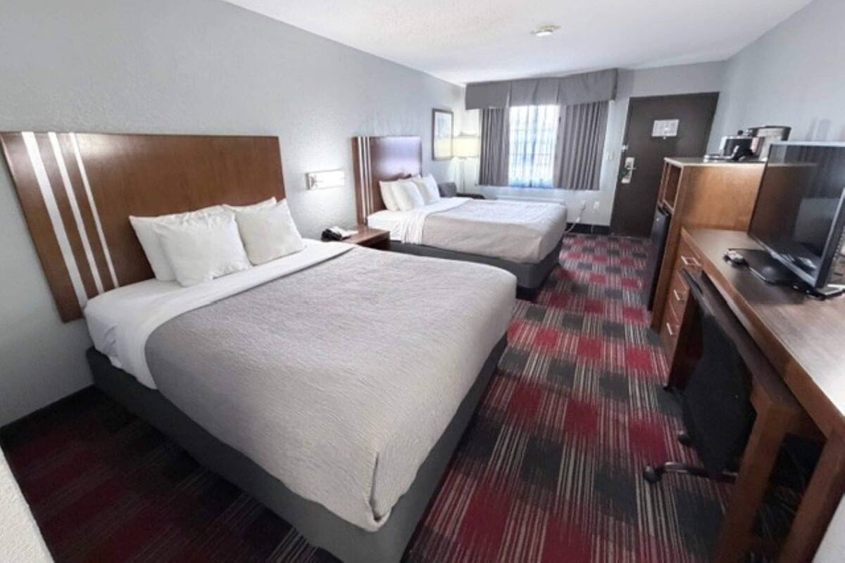 Quarto de hotel com duas camas, uma escrivaninha, uma televisão e um tapete estampado.