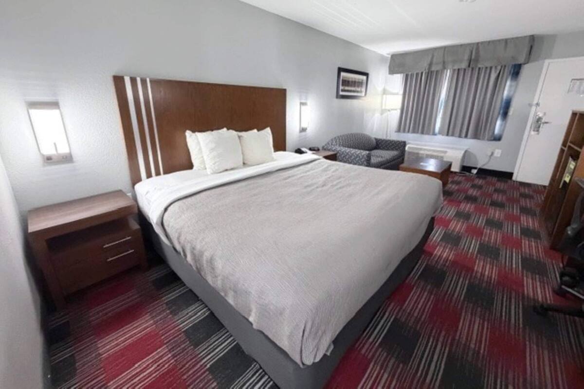 Quarto de hotel com uma cama grande, mesa de cabeceira, cadeira, escrivaninha e guarda-roupa.