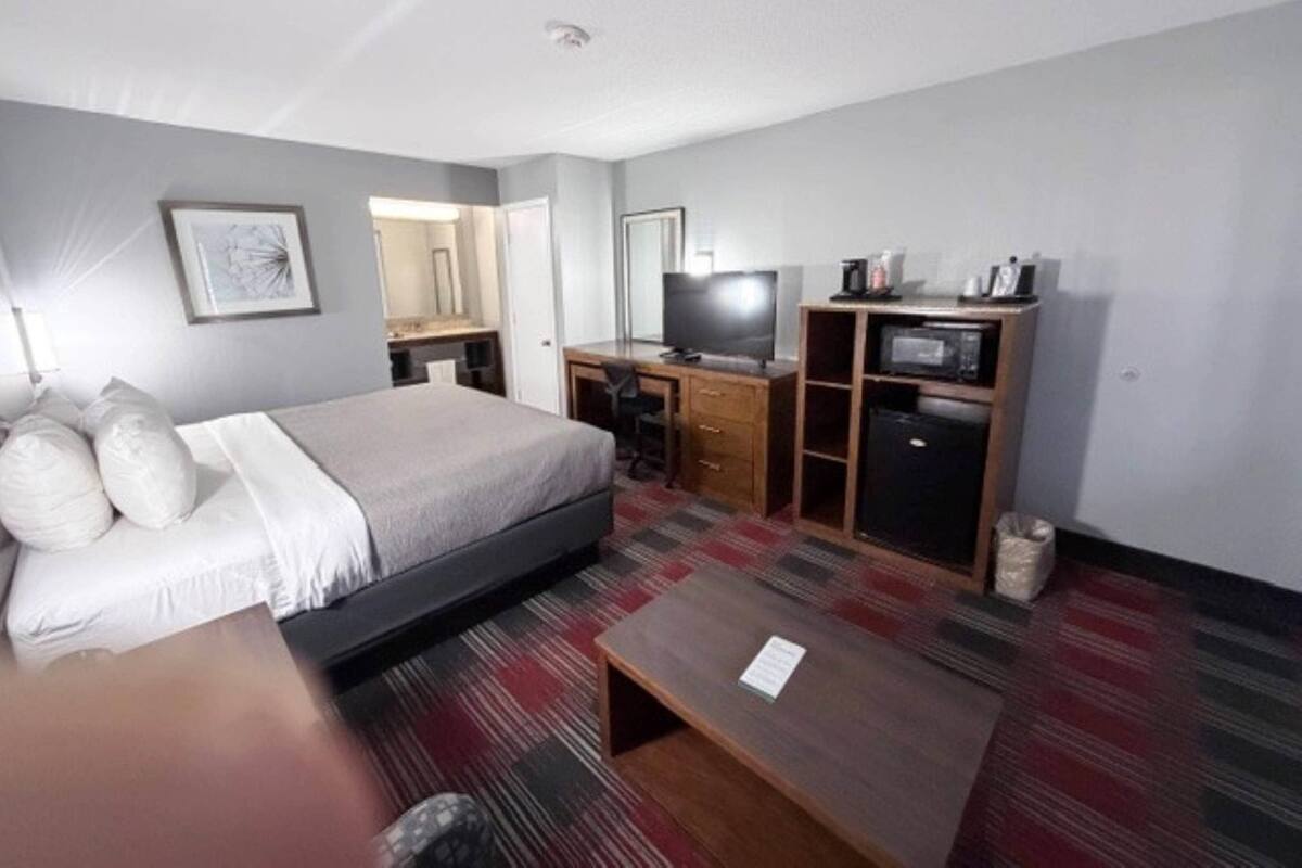 Quarto de hotel com uma cama, uma escrivaninha com computador, televisão e micro-ondas.