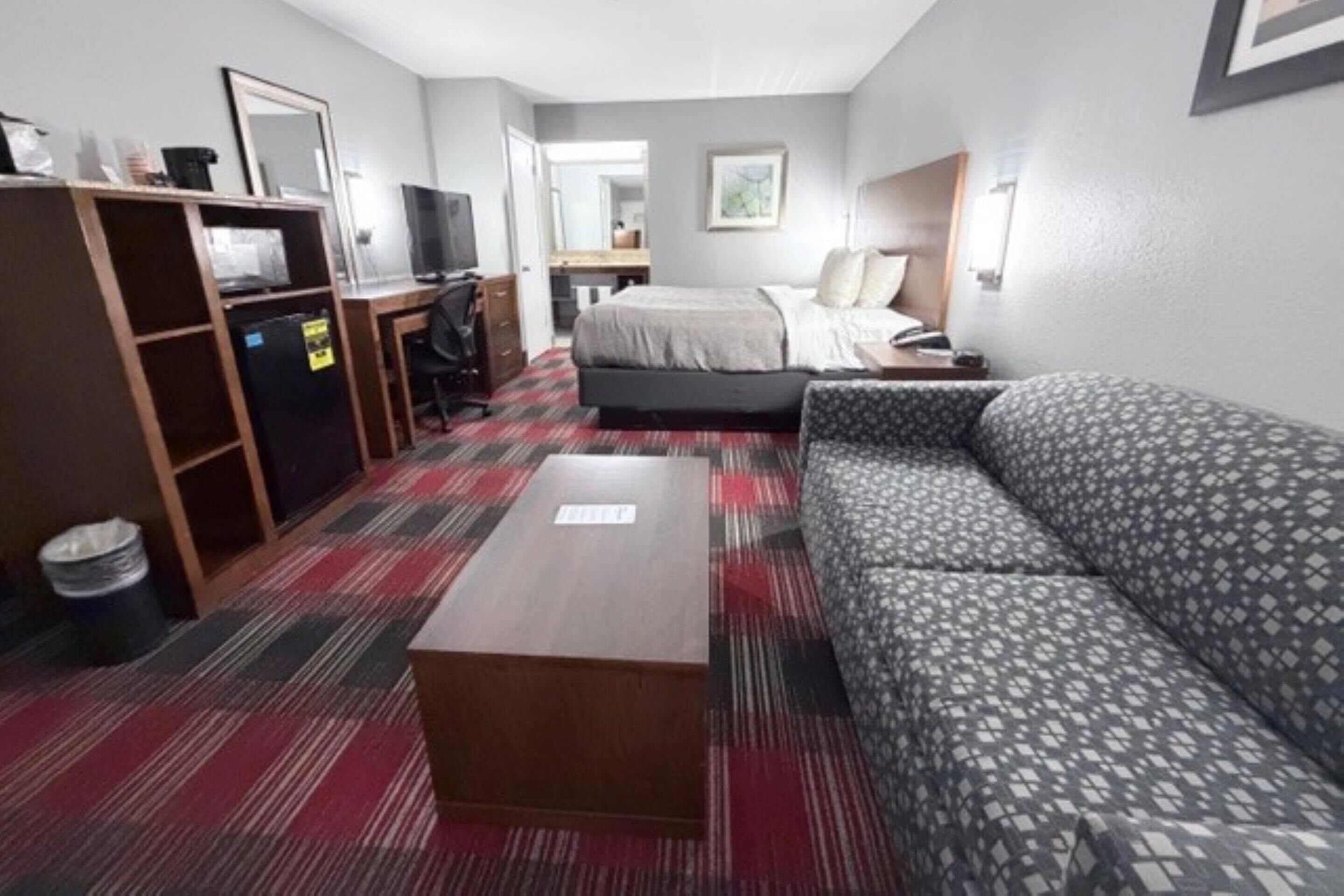 Quarto de hotel com cama, sofá, escrivaninha com computador, televisão e espelho.