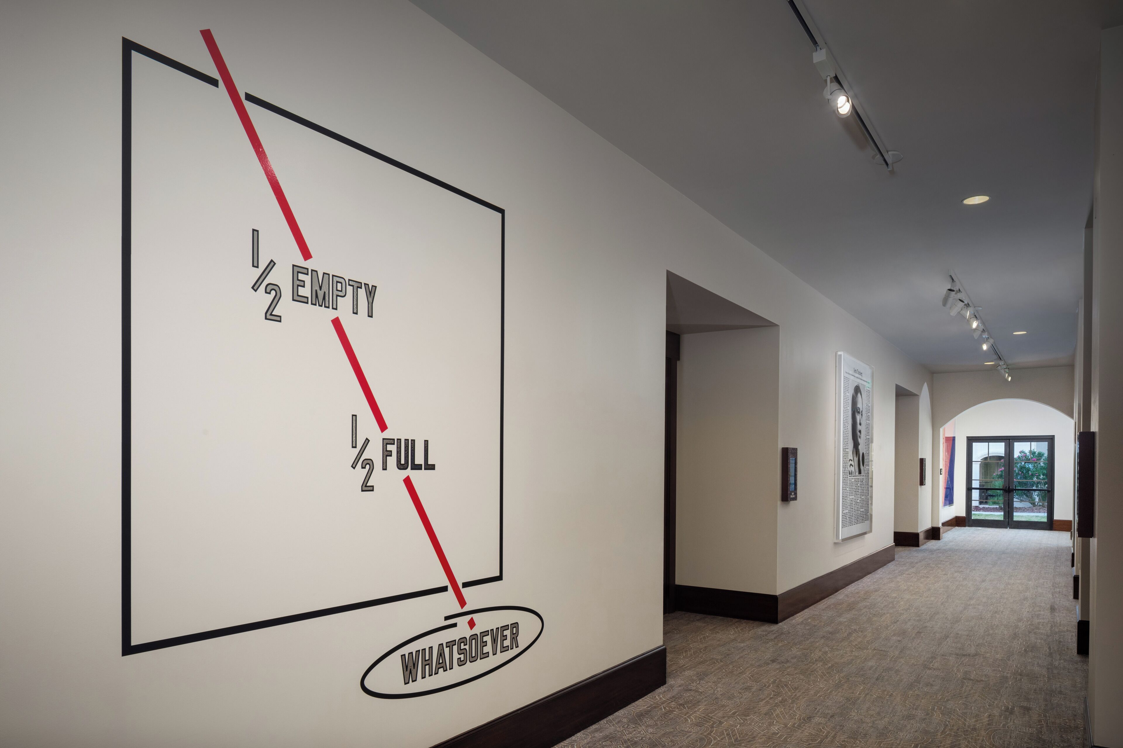 Um corredor com um diagrama fixado na parede mostrando os níveis de ocupação, um quadro emoldurado e uma porta no final.