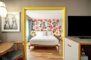 Quarto de hotel com cama, televisão, escrivaninha e cadeira.