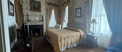 Quarto com uma cama grande, lareira, escrivaninha e poltrona azul.