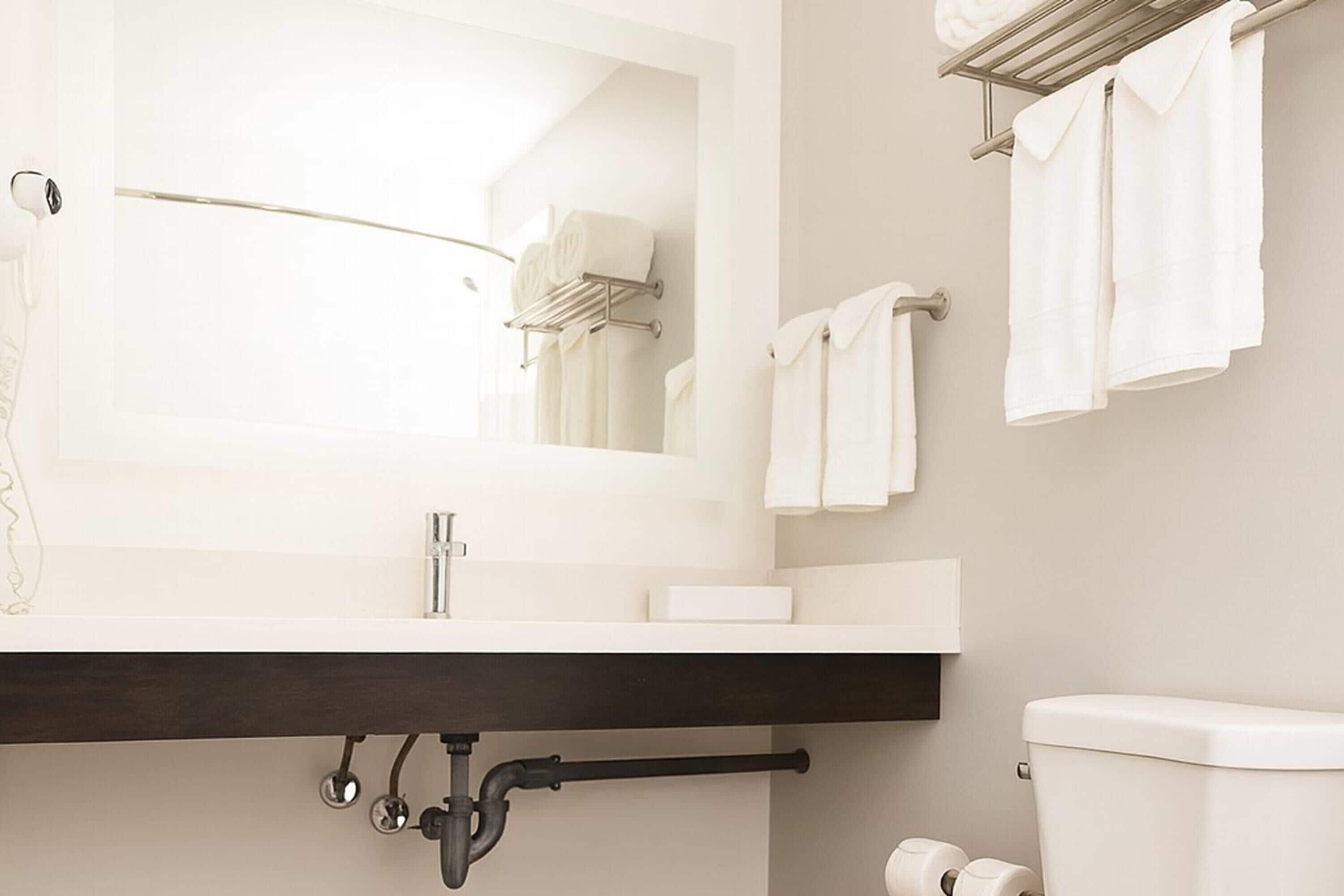 Casa de banho moderna com lavatório branco, bancada escura e sanita com dispensador de papel.