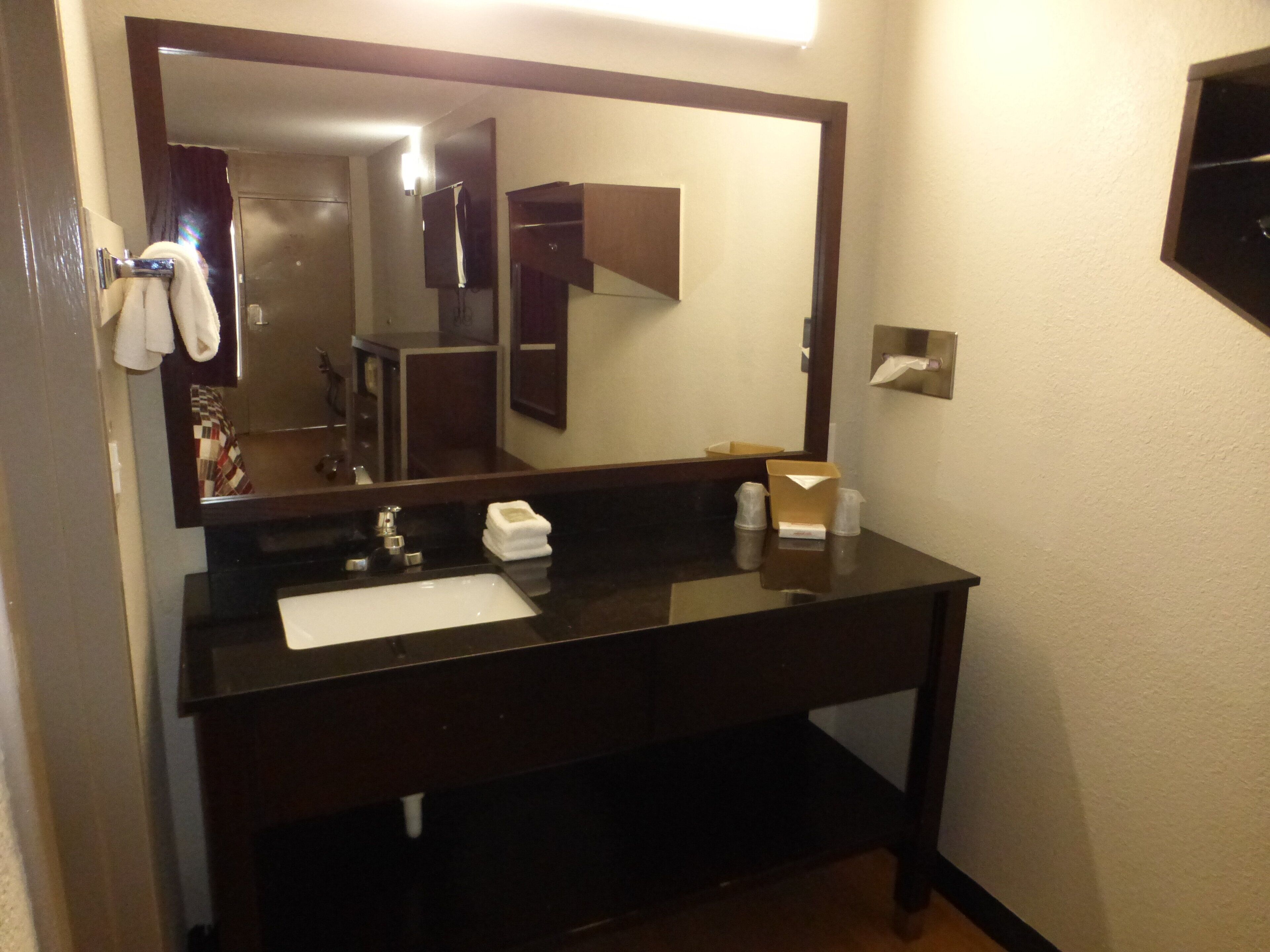 Uma casa de banho de hotel com uma toucador de madeira escura, um espelho grande, uma sanita branca e um porta-toalhas.