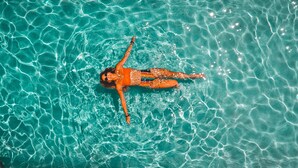 Uma pessoa flutuando em uma piscina azul translúcida, com ondulações e reflexos visíveis.