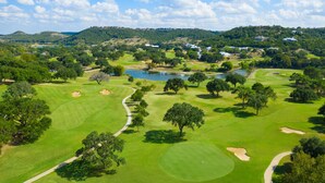 Um campo de golfe com vários fairways, bunkers de areia e um lago.