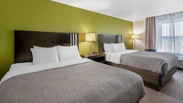 Quarto de hotel com duas camas, paredes verdes e uma janela com cortinas.
