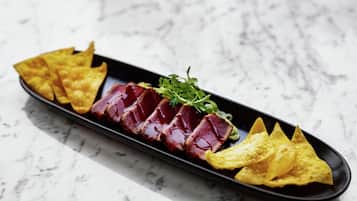 Prato retangular preto com carne vermelha fatiada, guarnição verde e batatas fritas amarelas.