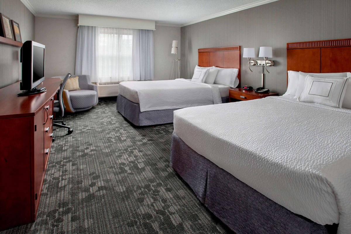 Quarto de hotel com duas camas, uma mesa, uma televisão e uma cadeira.