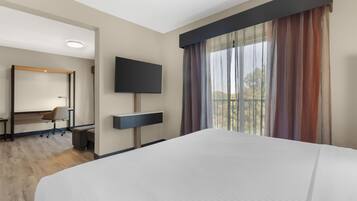 Quarto de hotel com uma cama grande, uma escrivaninha com cadeira, televisão de tela plana na parede e uma janela com cortinas.