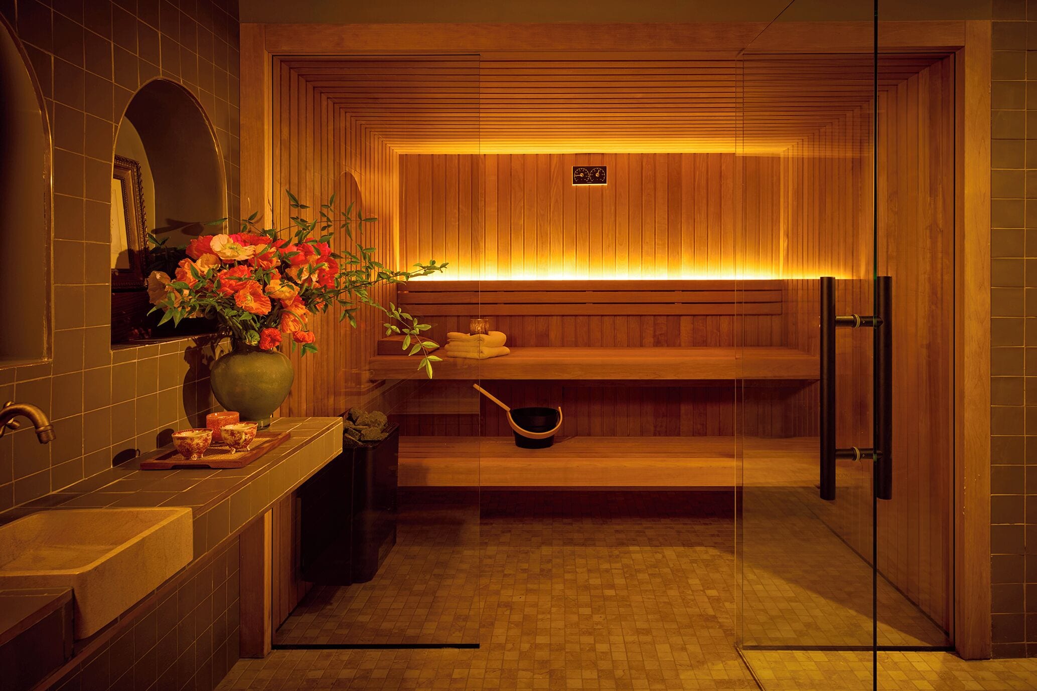 Uma sauna com paredes de madeira, um banco e uma pequena mesa com uma tigela e um vaso de flores.