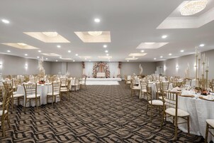 Uma sala de banquetes com mesas redondas, cadeiras e palco com decoraç ão floral.